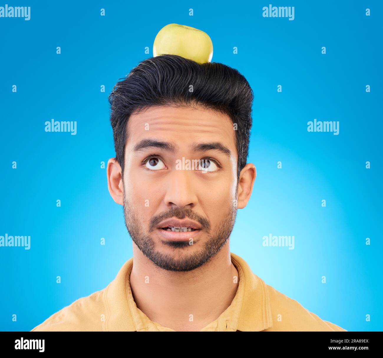 Man, thinking or balance apple on head in studio isolated on a blue ...