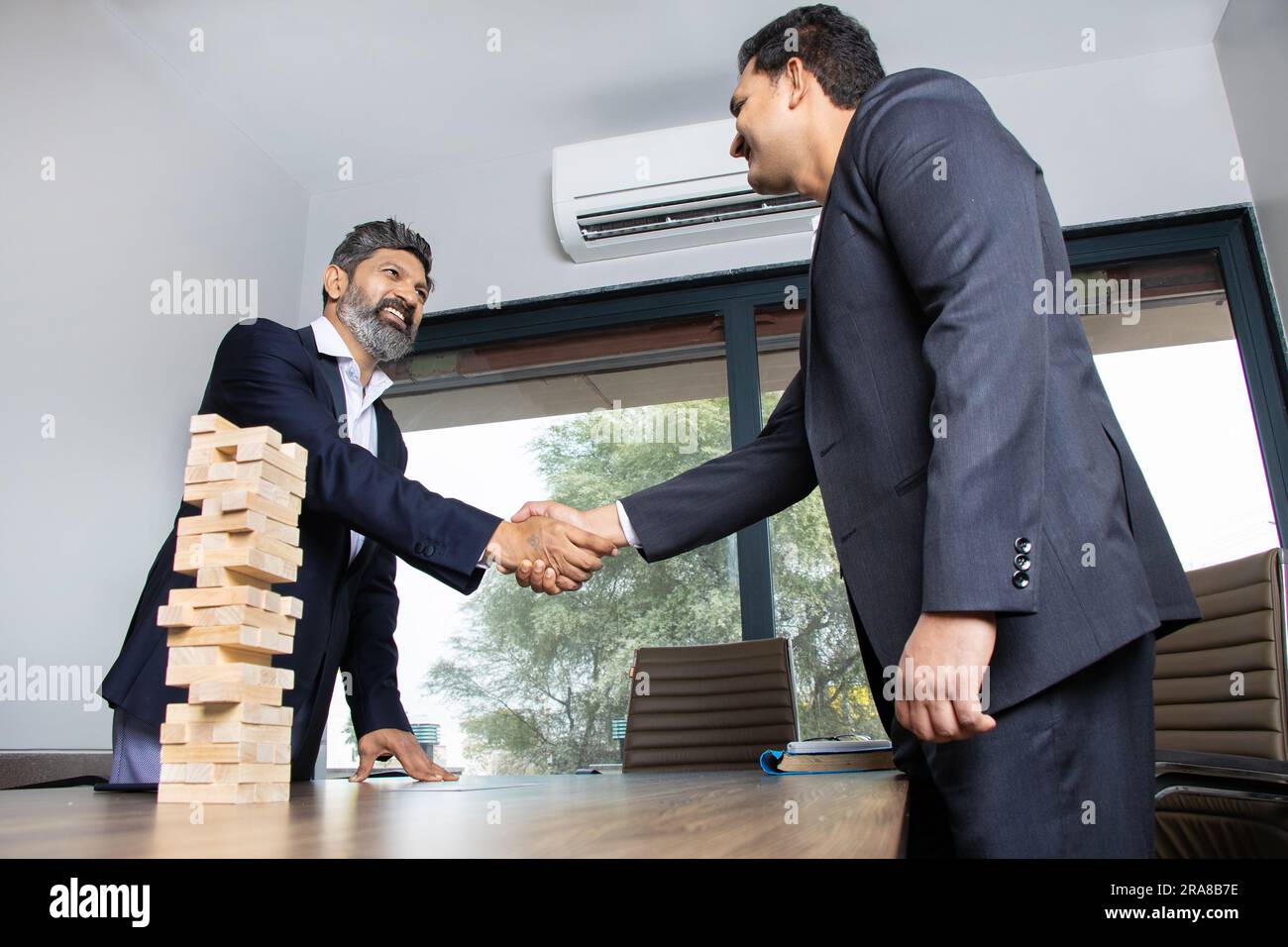 Two indian businessman shake hands while standing near wooden block ...