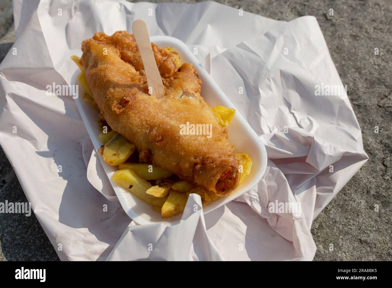 Fish and chips, battered cod, in a tray wrapped in paper with a wooden ...