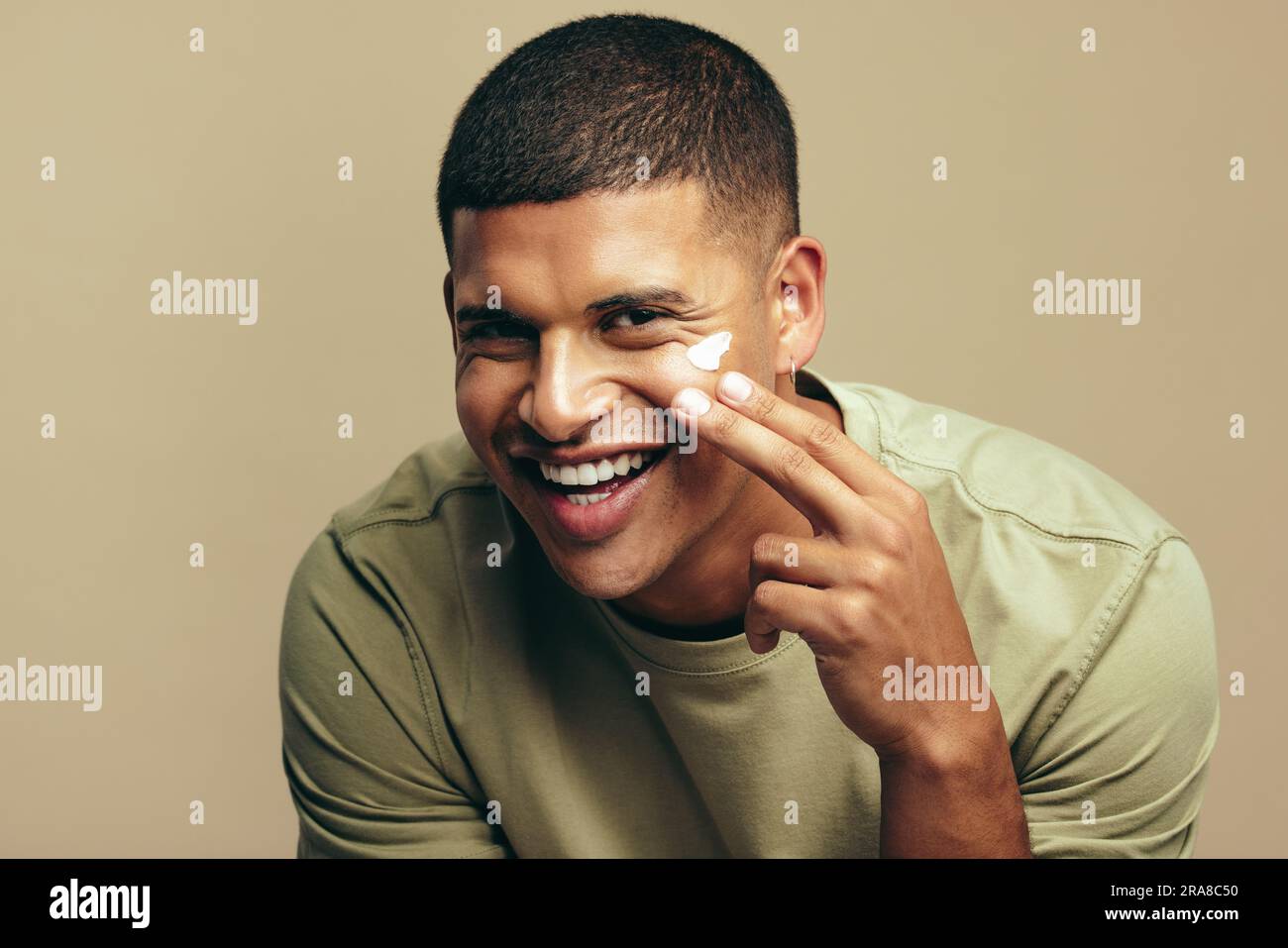 Portrait of a happy young man applying a beauty product on his face ...