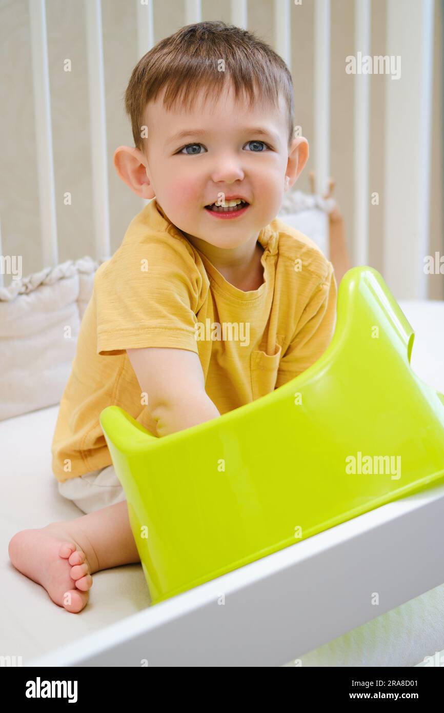 A toddler baby with a children toilet potty is sitting in a crib ...