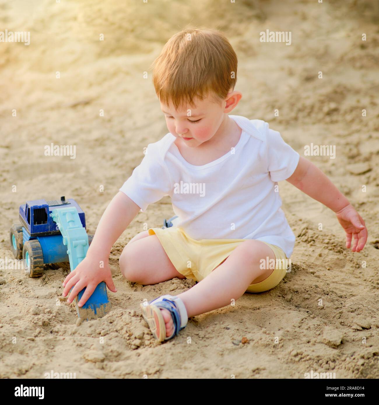 Baby boy is playing with a toy excavator sitting in the sandbox. A ...