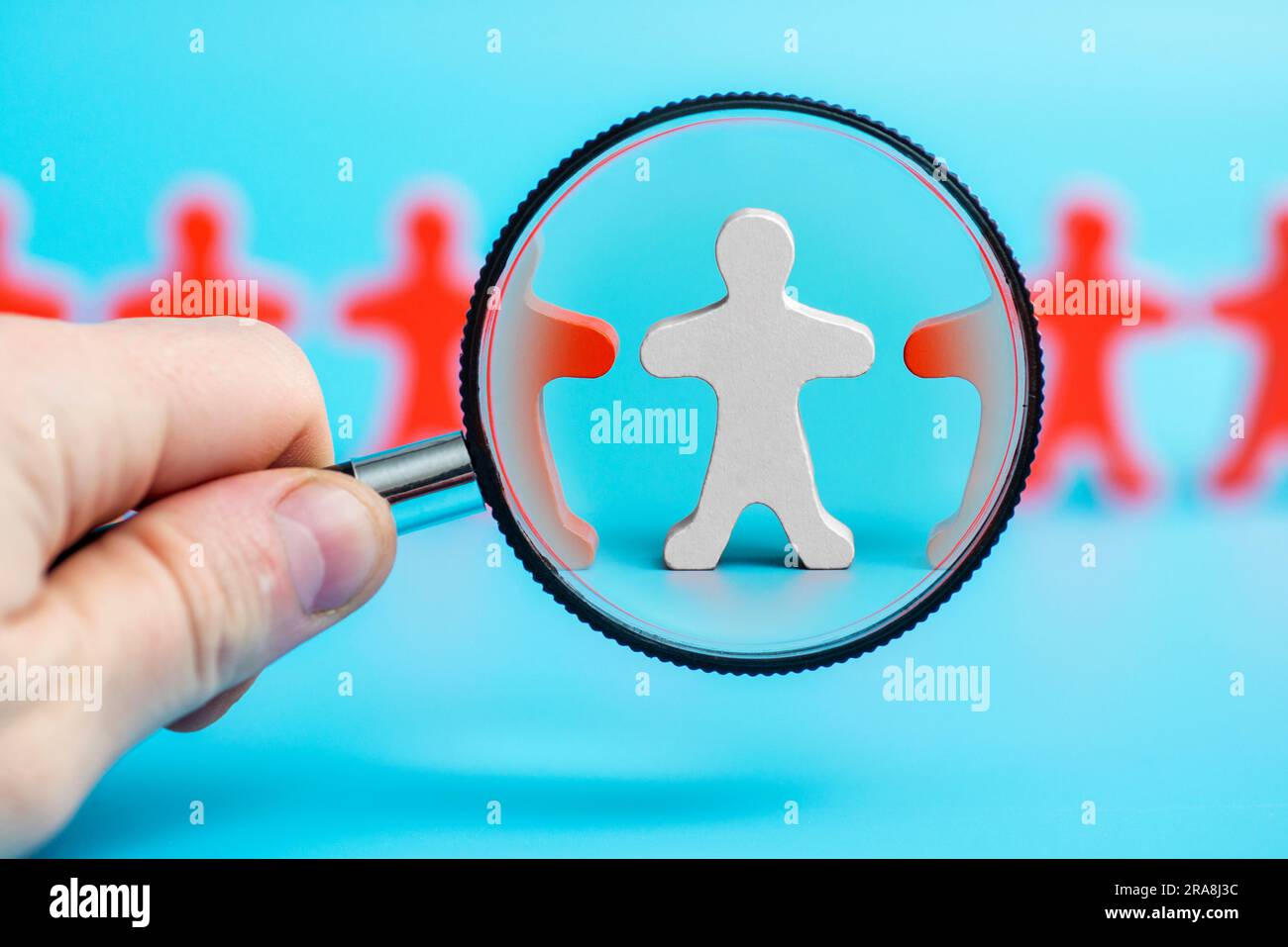 A mans hand with a magnifying glass is aimed at row of wooden figures ...
