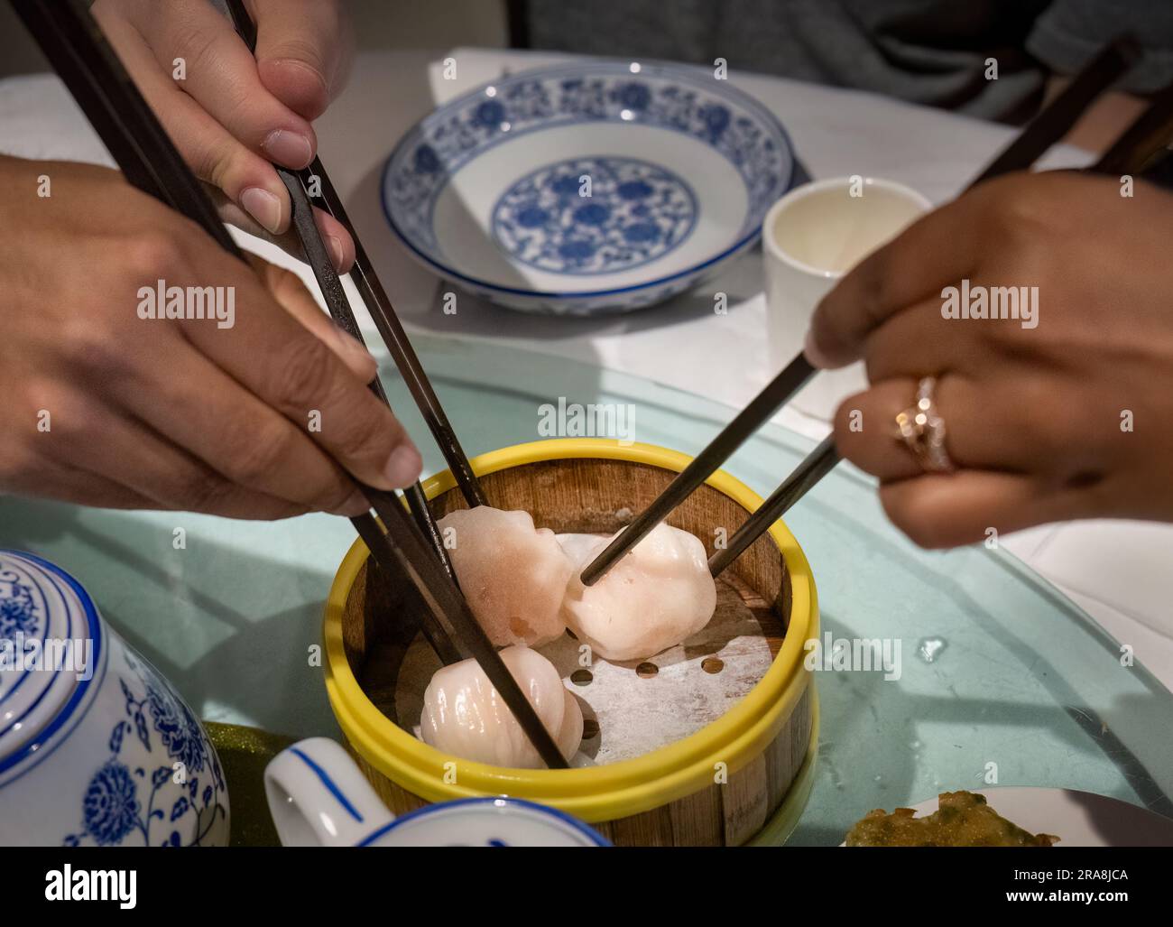 Yumcha, dim sum in bamboo steamer. Hands holding chopsticks for ...