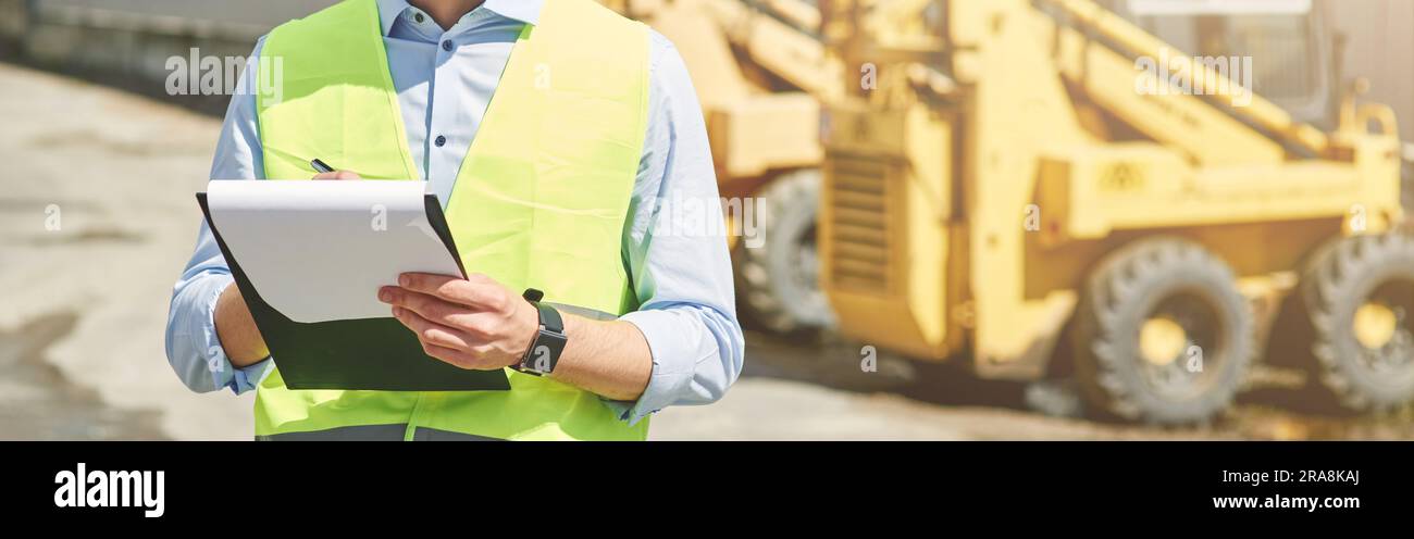 Young civil engineer wearing helmet writing report while standing at ...