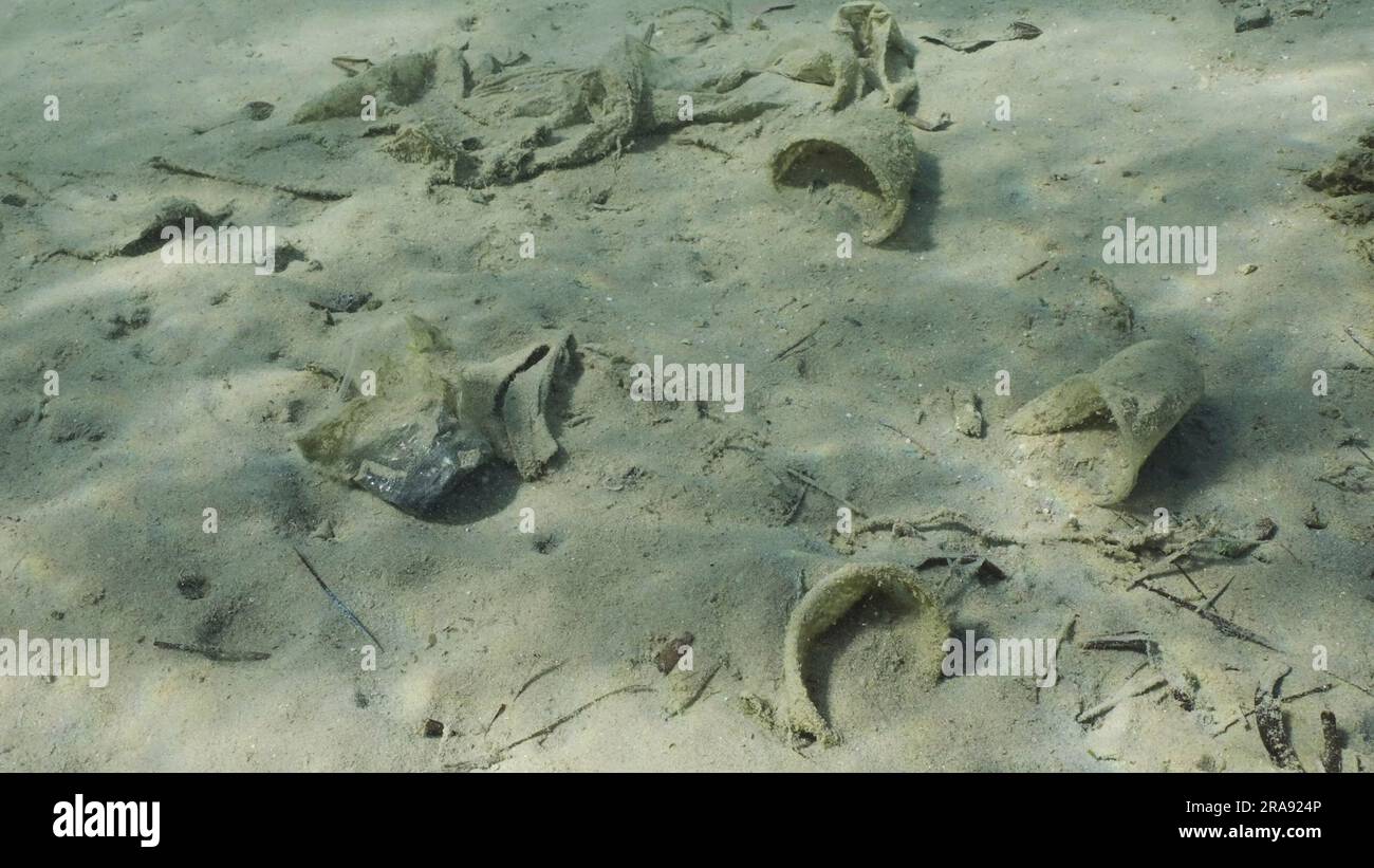 Plastic garbage lies on sandy-silty bottom of sea in shallow water on ...