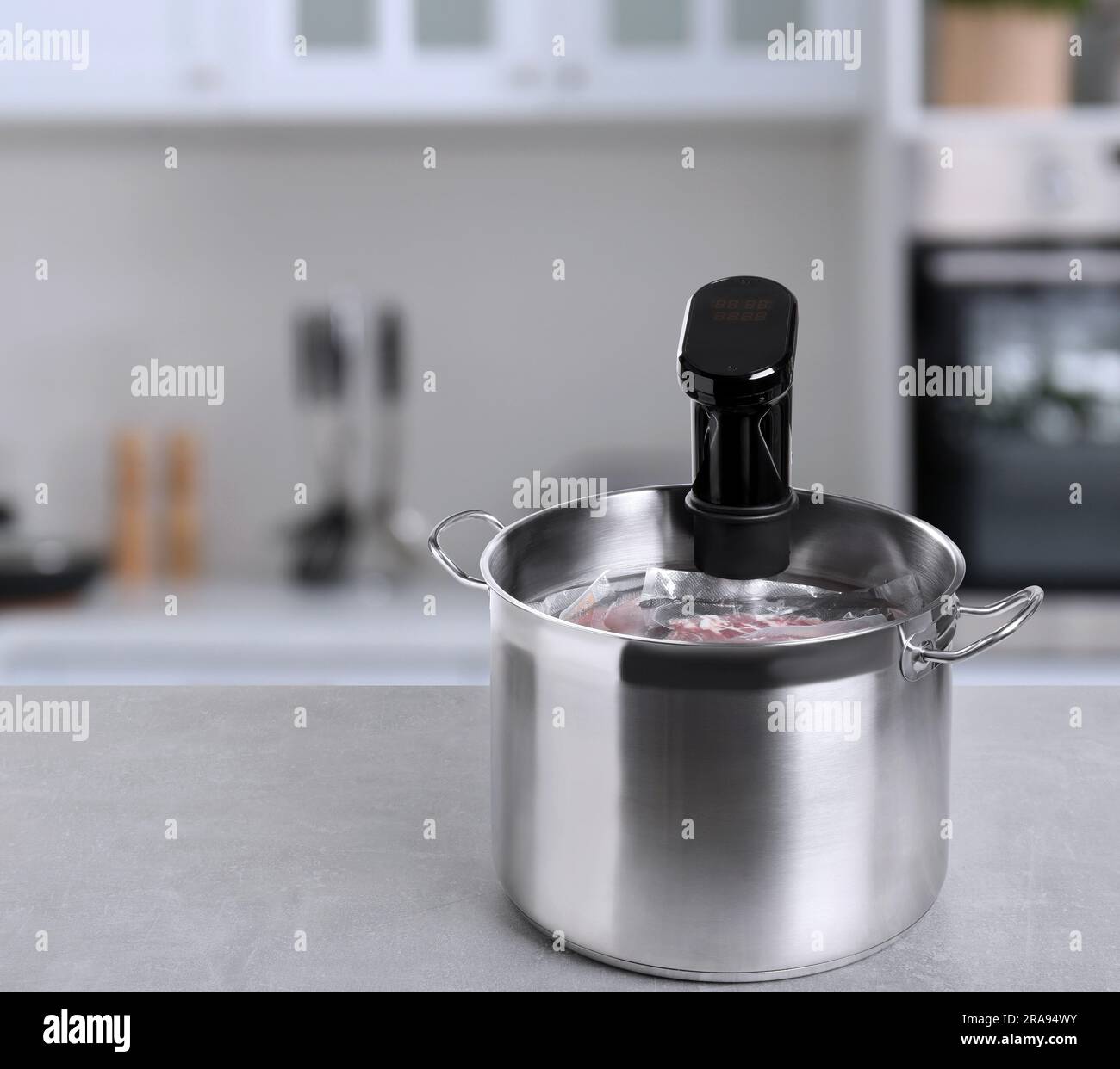 Sous vide cooker and vacuum packed food products in pot on light marble ...