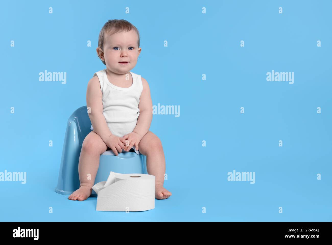 Little child sitting on baby potty and toilet paper roll against light ...