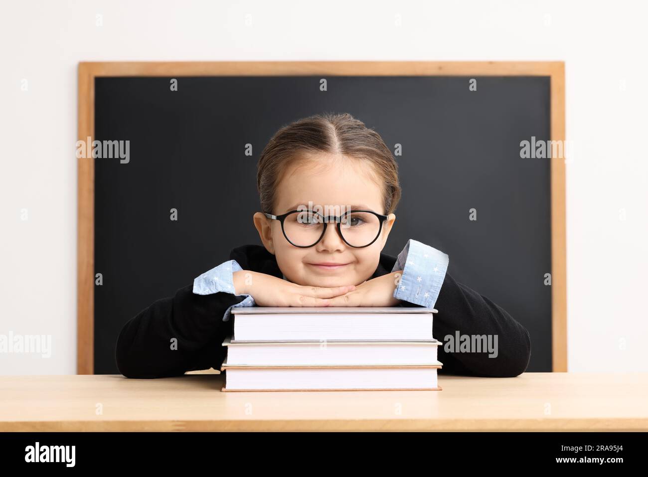 Happy little school child sitting at desk with books near chalkboard in ...