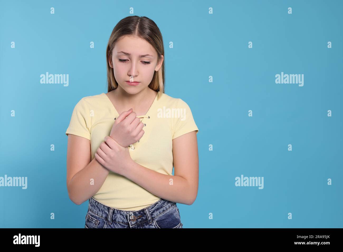 Teenage girl suffering from pain in wrist on light blue background ...