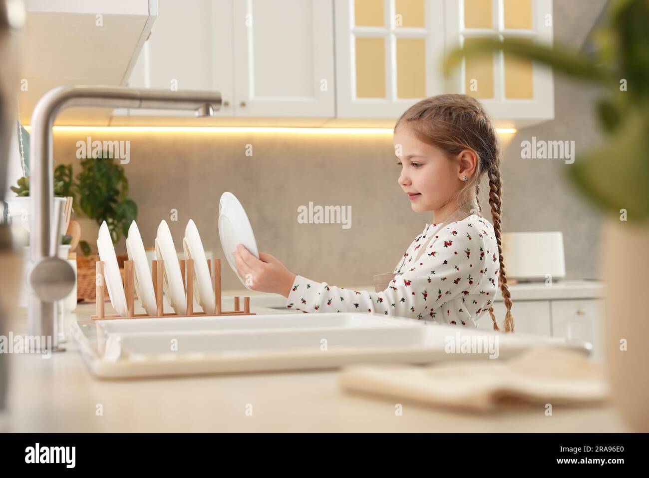 Girl putting clean plate on drying rack in kitchen Stock Photo - Alamy