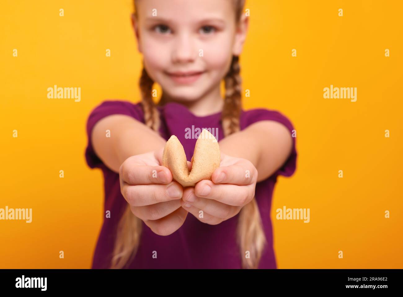 Cute girl holding tasty fortune cookie with prediction on orange background, selective focus ...