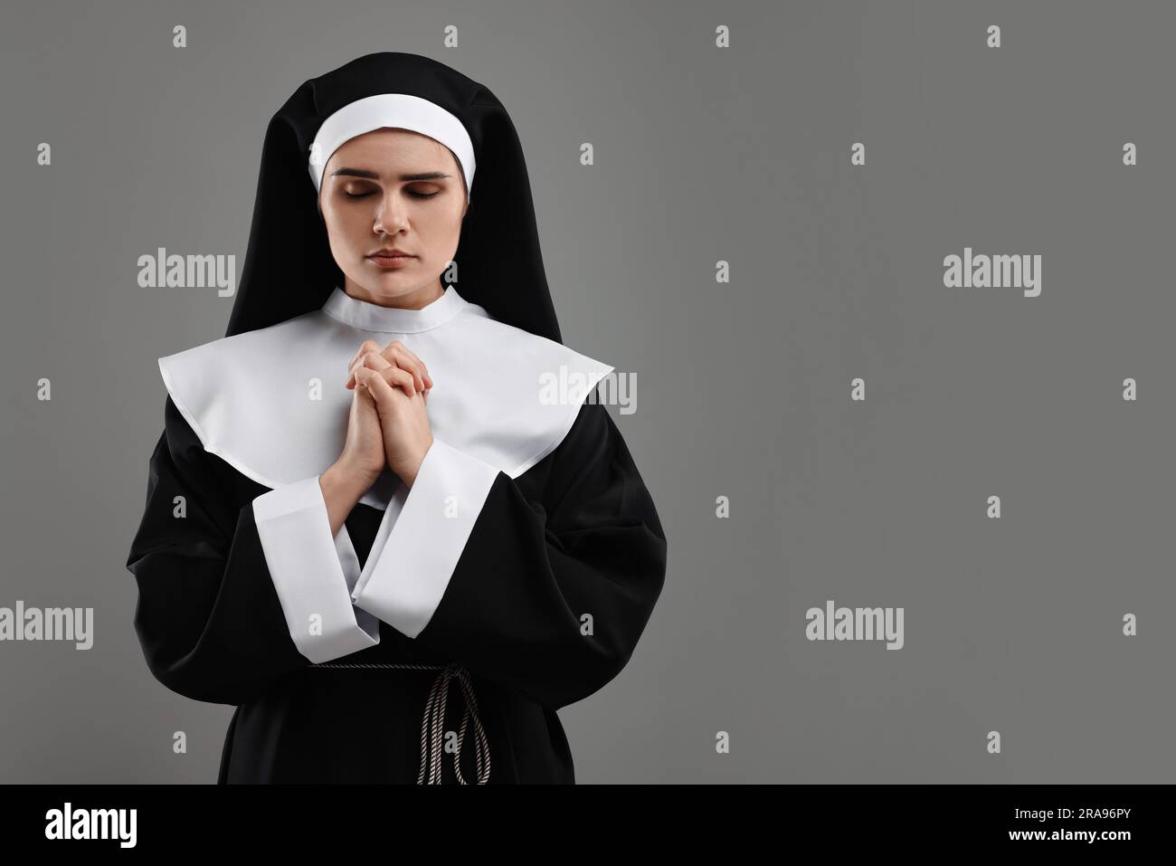 Nun with clasped hands praying to God on grey background. Space for ...