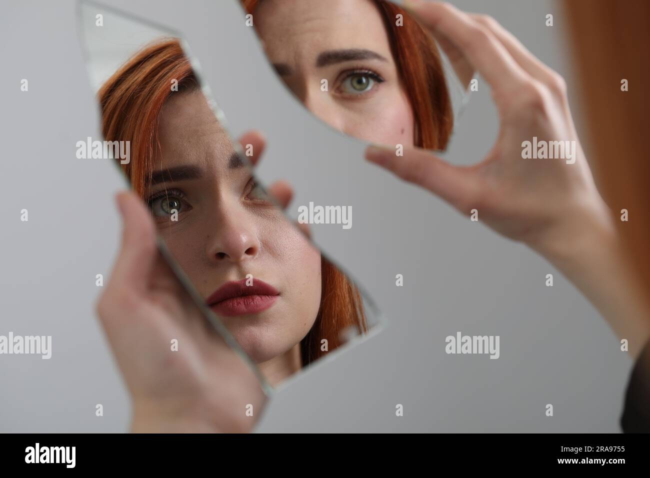 Young woman looking at herself in shard of broken mirror on light grey ...