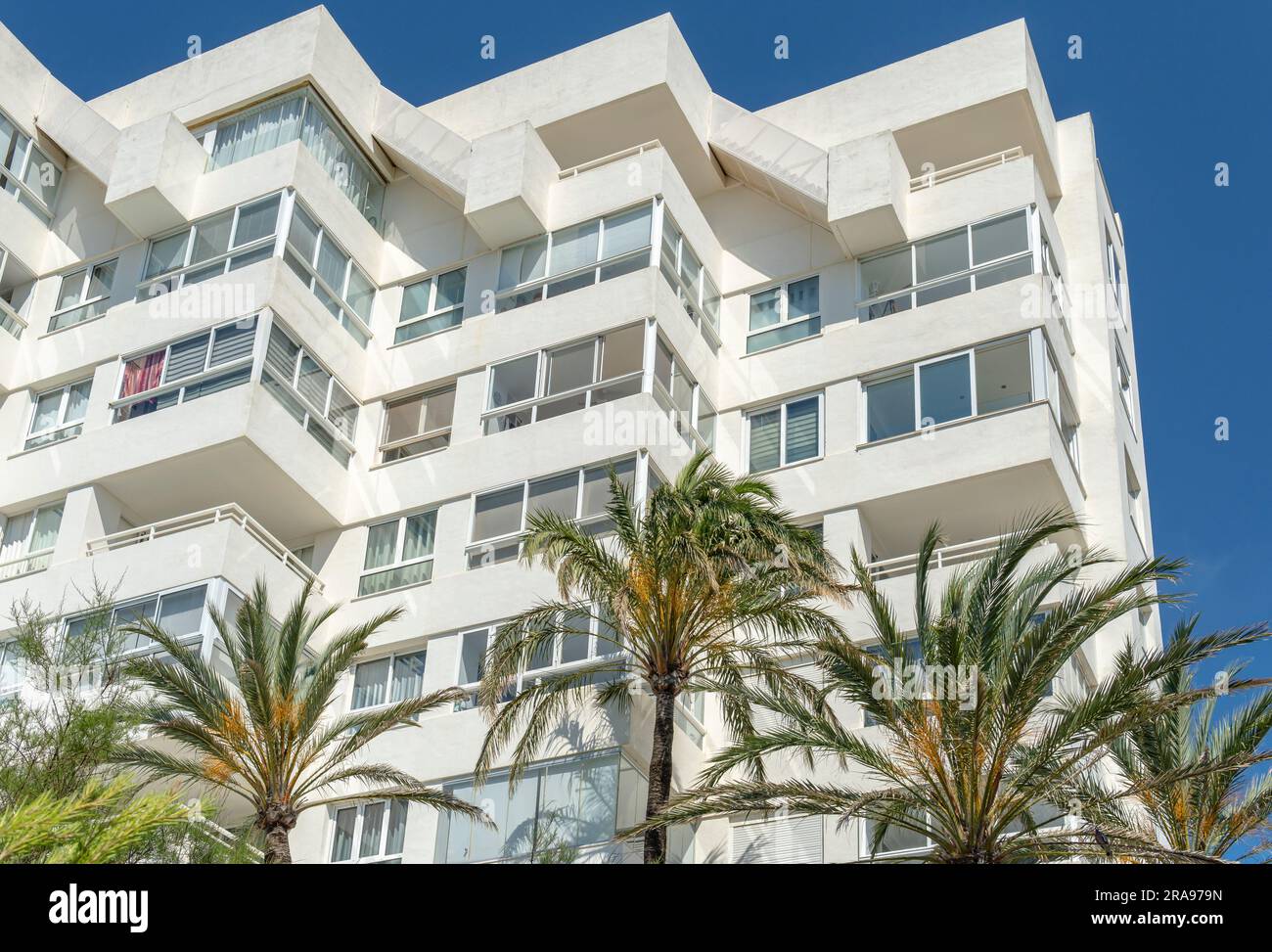 Facade of a white tourist apartment building with palm trees. Island of ...