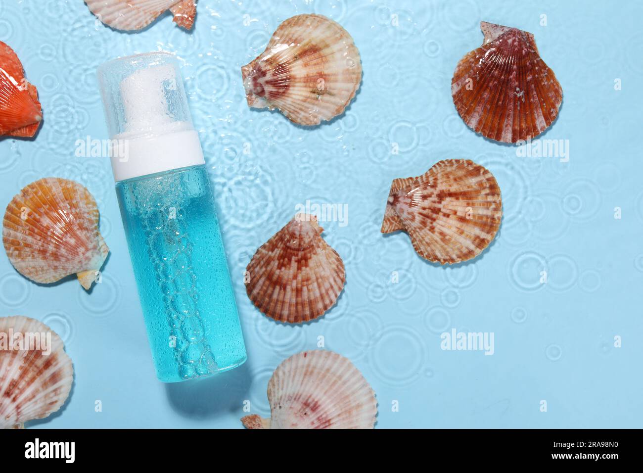 Bottle of face cleansing product and seashells in water against light ...