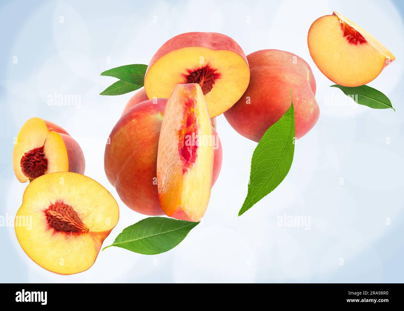 Cut and whole fresh ripe peaches with green leaves falling on light ...