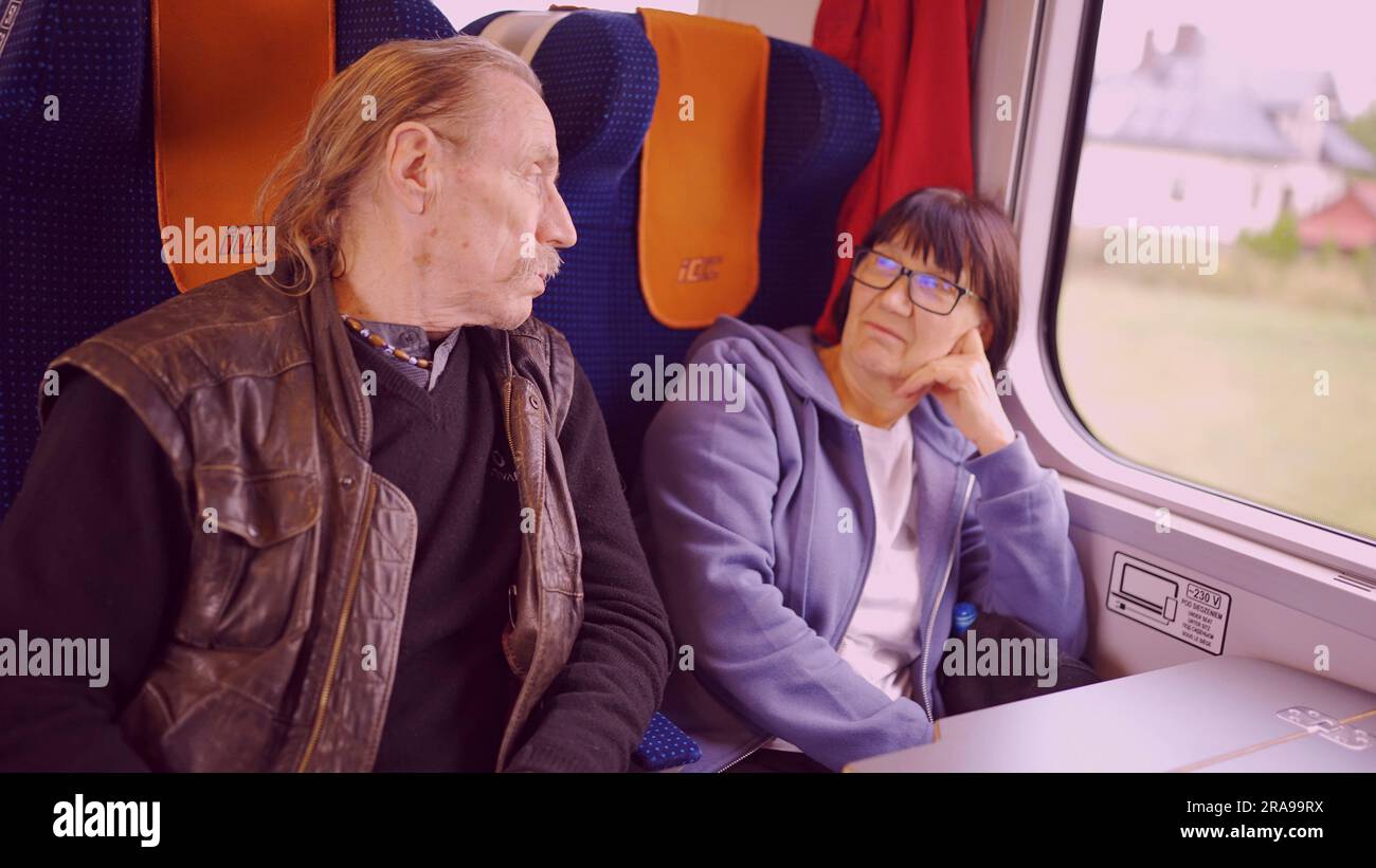 Elderly couple is riding in a train carriage and talking with each ...