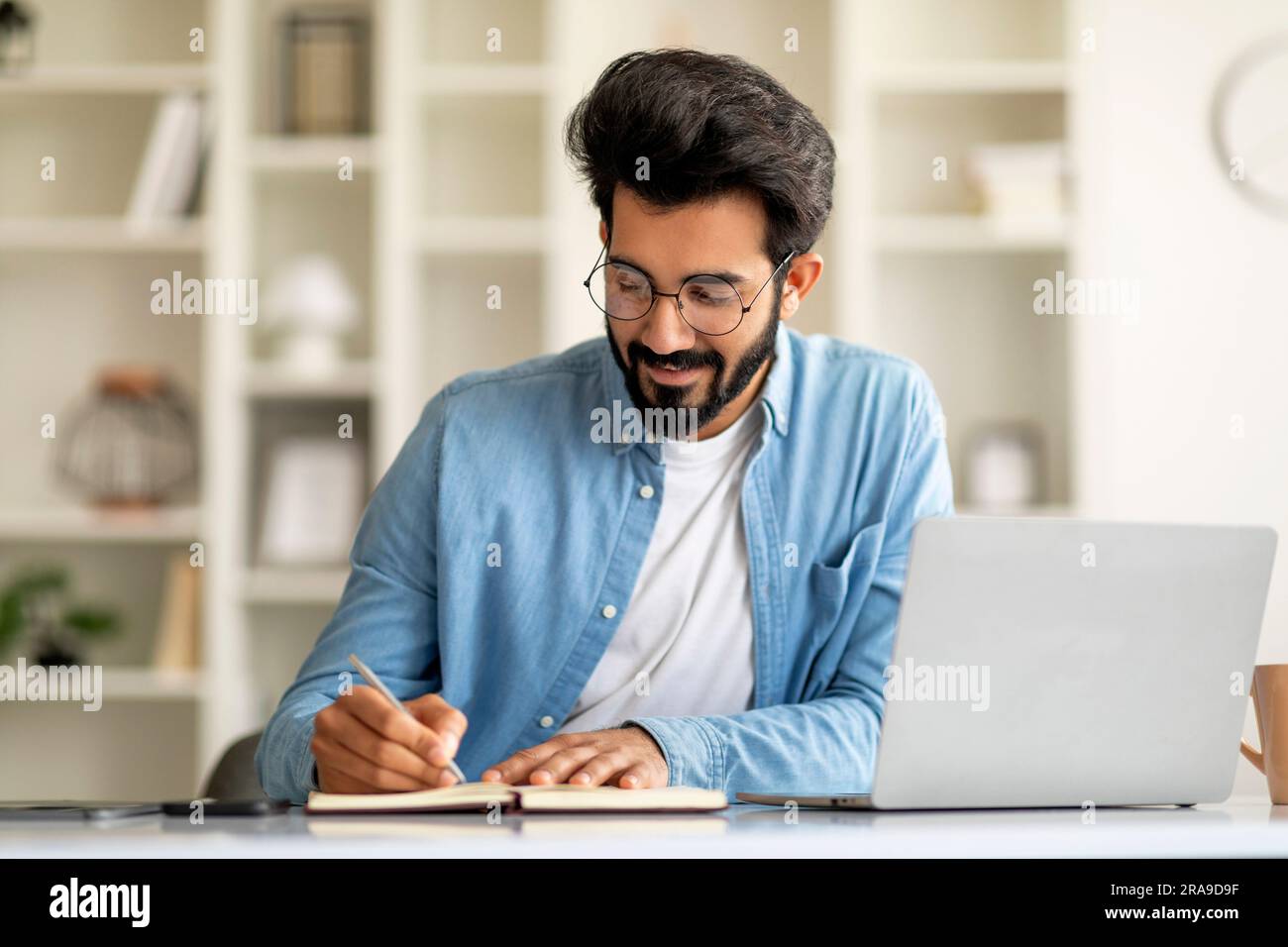 Smiling Indian Man Taking Notes While Working With Laptop At Home ...