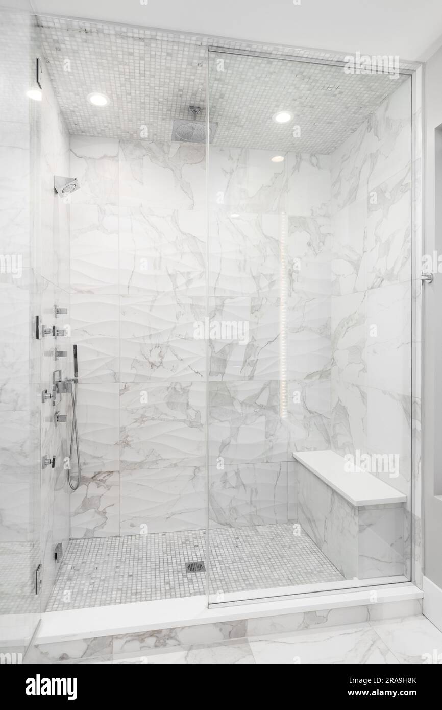 A walk-in shower with wavy marble pattern tiles, chrome faucets, and a ...