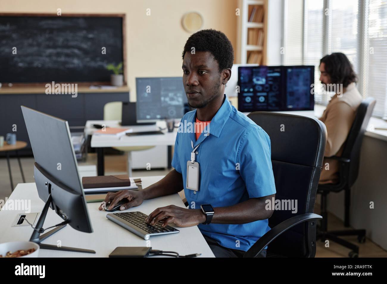 Young serious African American programmer sitting in front of computer monitor, looking at ...