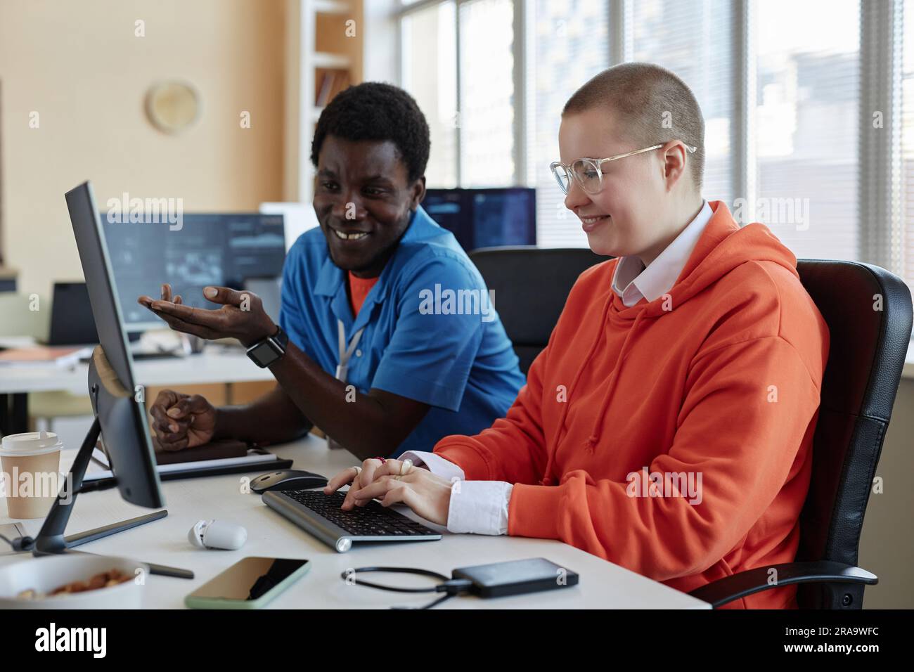 Two young intercultural colleagues discussing data on computer screen while smiling African ...