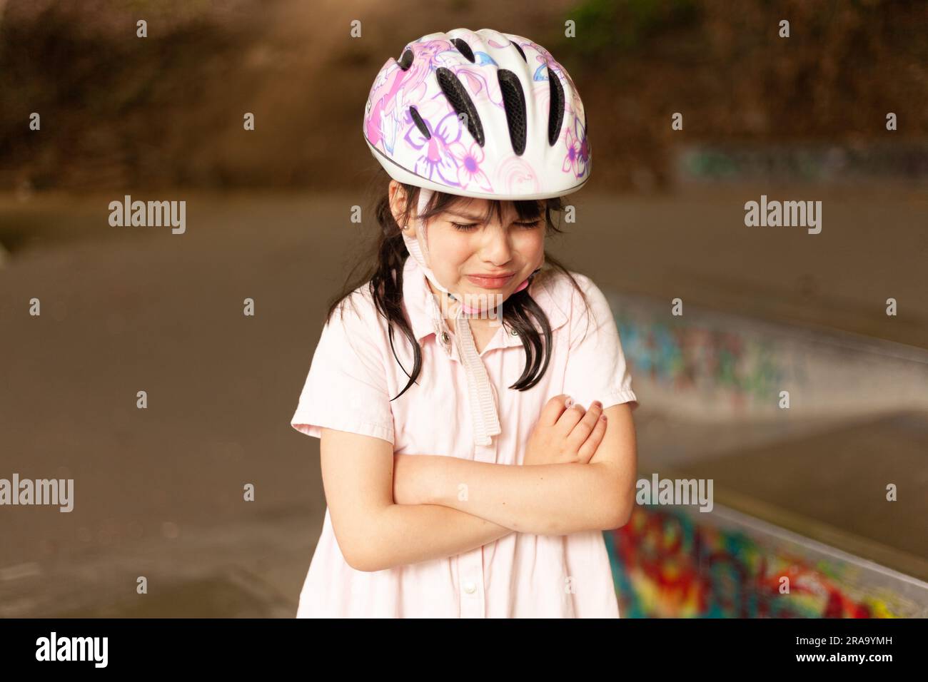 A little crying dark-haired girl cyclist in a bicycle helmet and in a ...