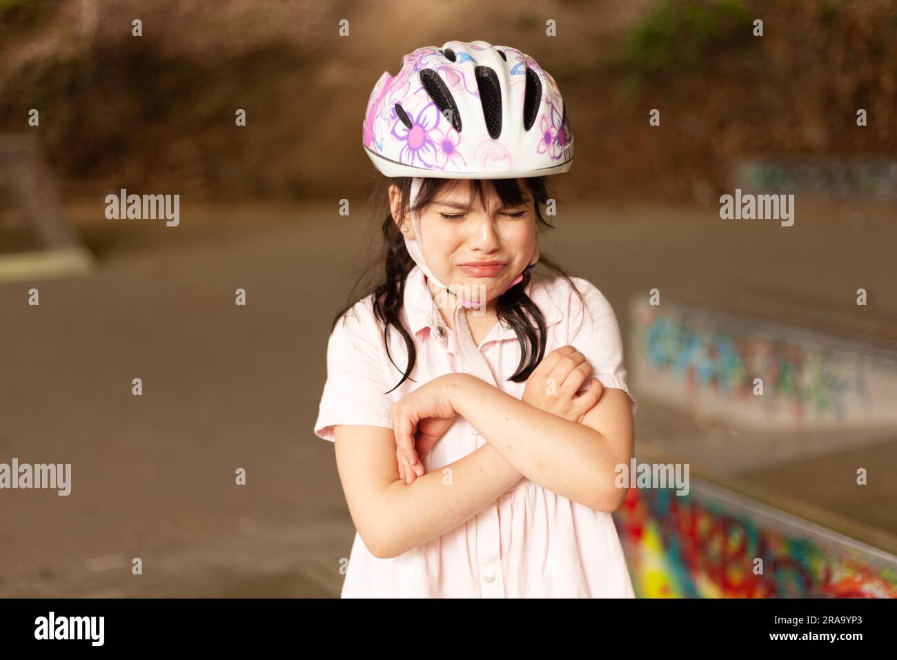 A little crying dark-haired girl cyclist in a bicycle helmet and in a ...