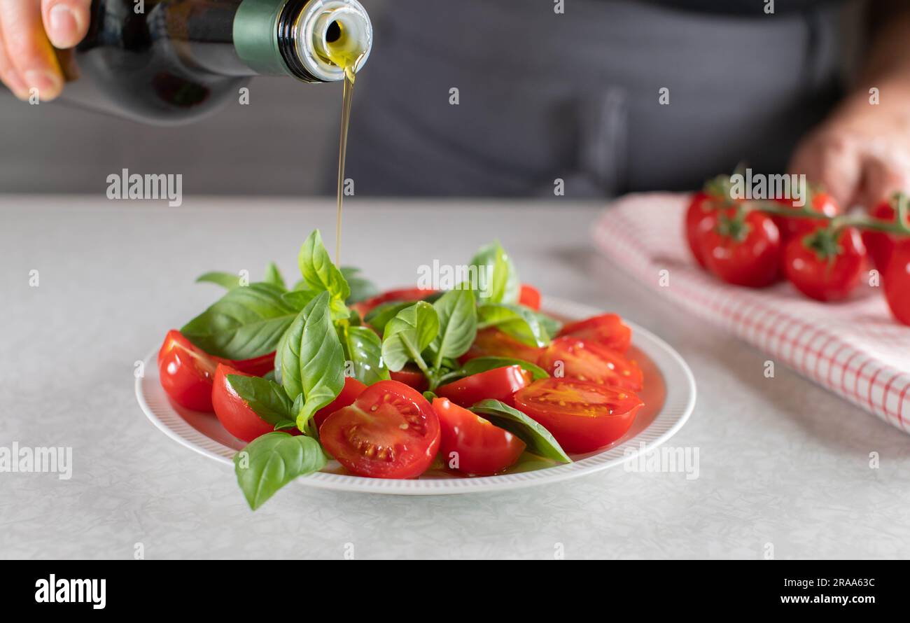 Pouring olive oil in a bottle over a cherry tomato salad with basil ...
