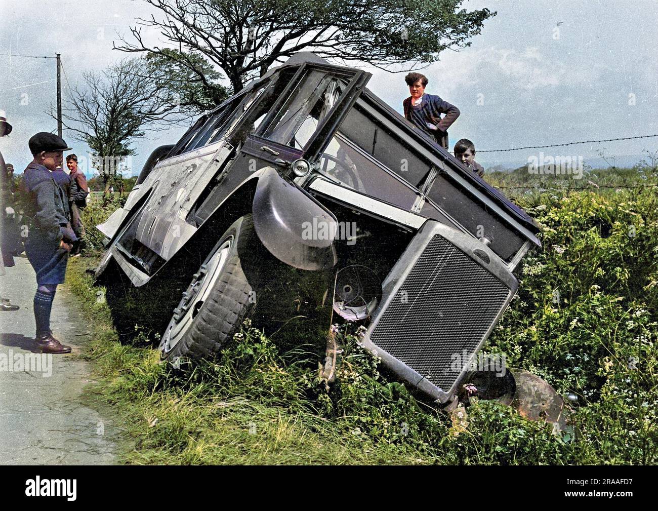 A bus which has somehow fallen into a ditch. A group of boys stand ...