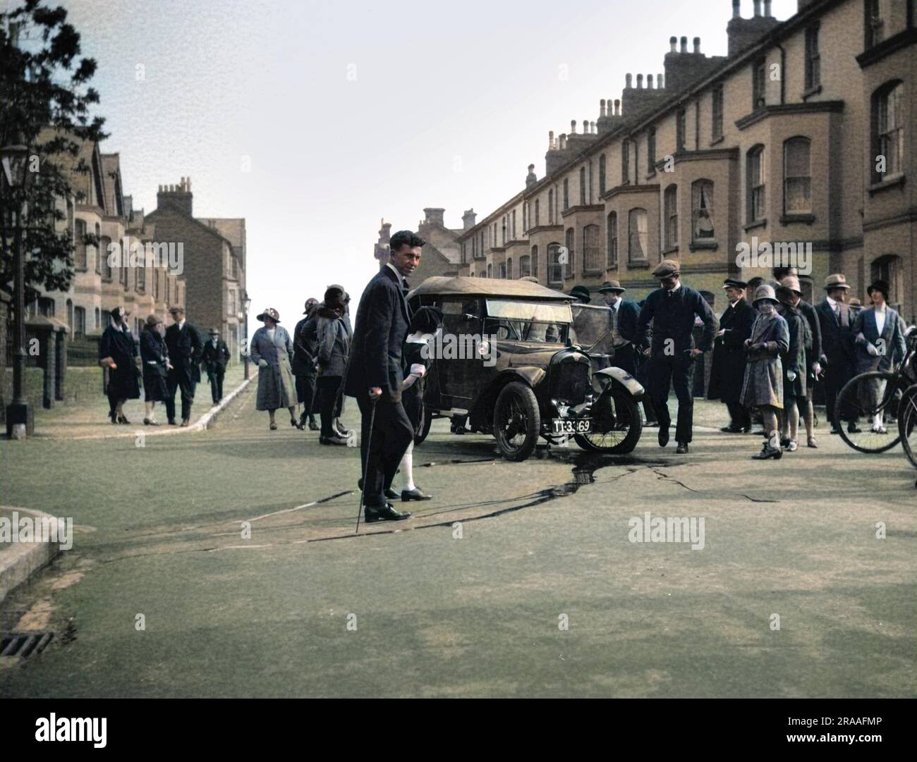 Street scene with people gathered round a damaged car. Water from the ...