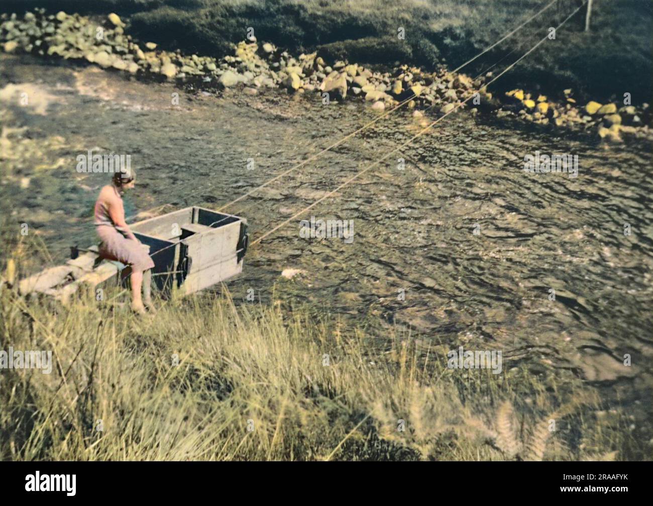 A woman pushing a box suspended by ropes across a river Stock Photo - Alamy