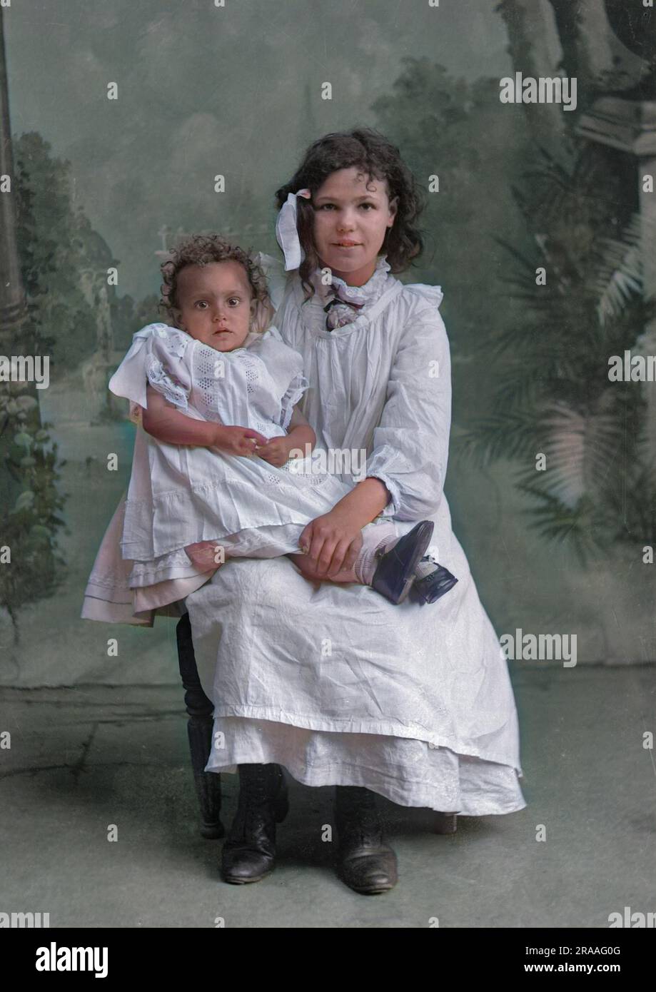 A young girl holding a toddler in a studio photo, with a painted ...