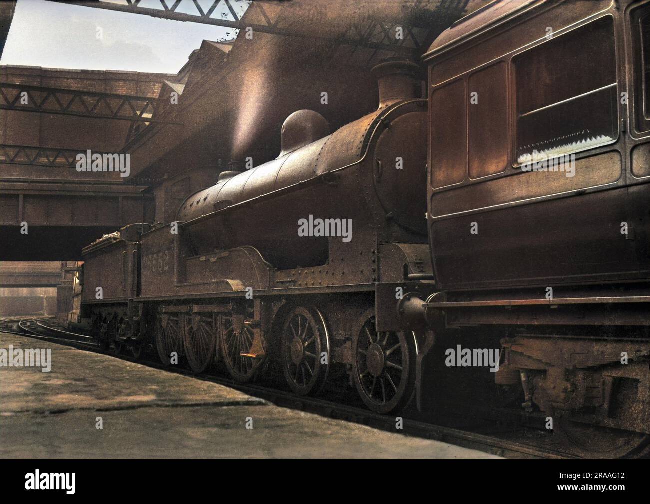 A steam engine with a passenger carriage attached, in a railway station ...