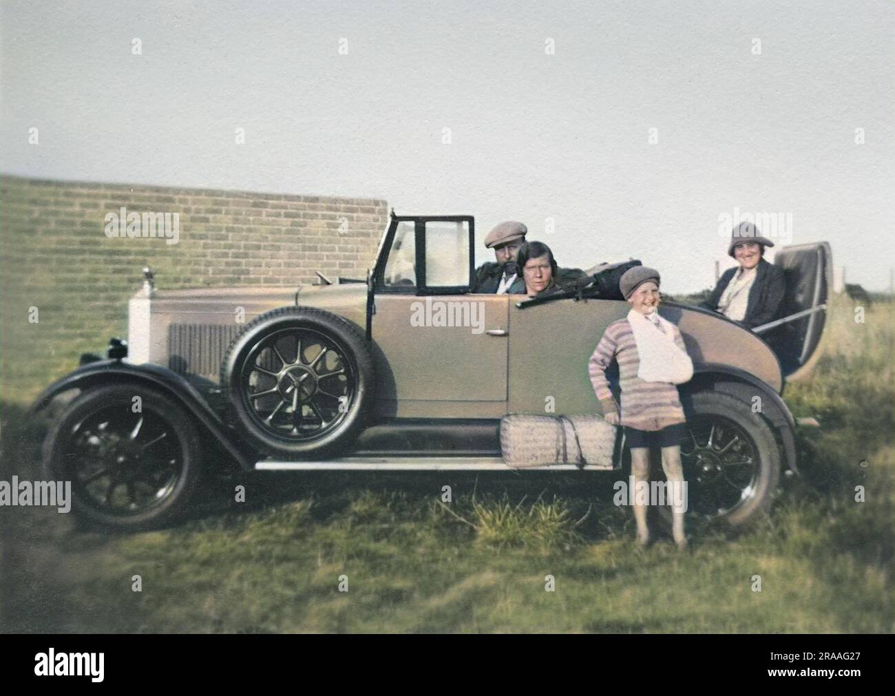 Three people sitting in an open-topped car. A smiling boy stands in ...