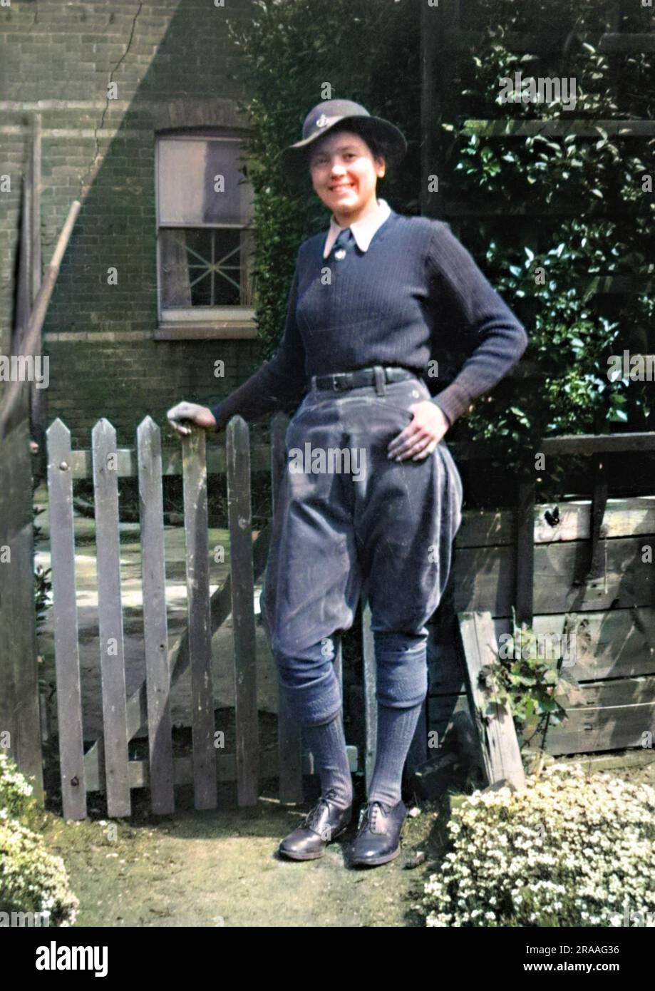 A member of the Women's Land Army (land girl) during the Second World War, standing by a garden ...