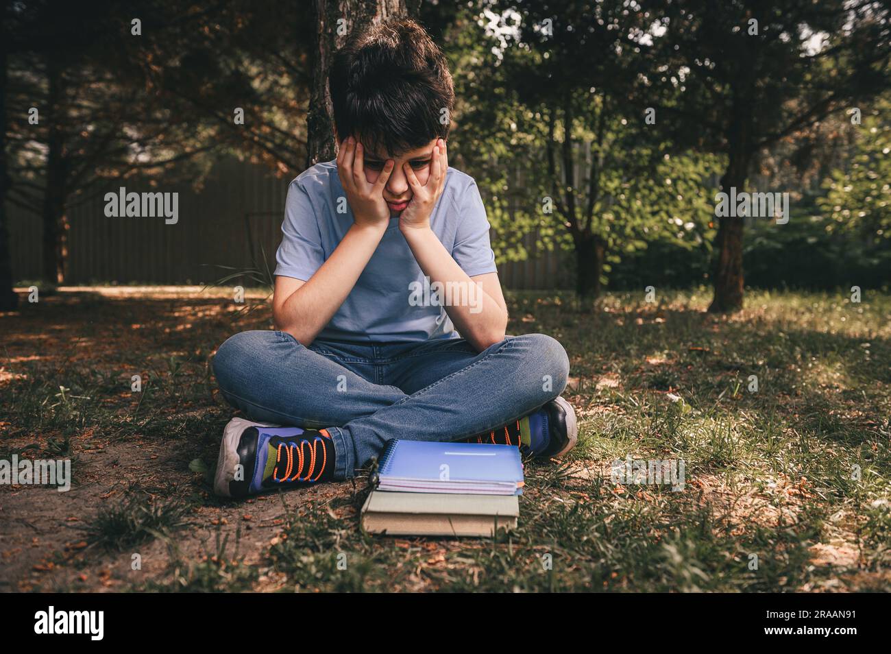 Lonely teen boy sitting in park with textbooks laid out, tired after ...
