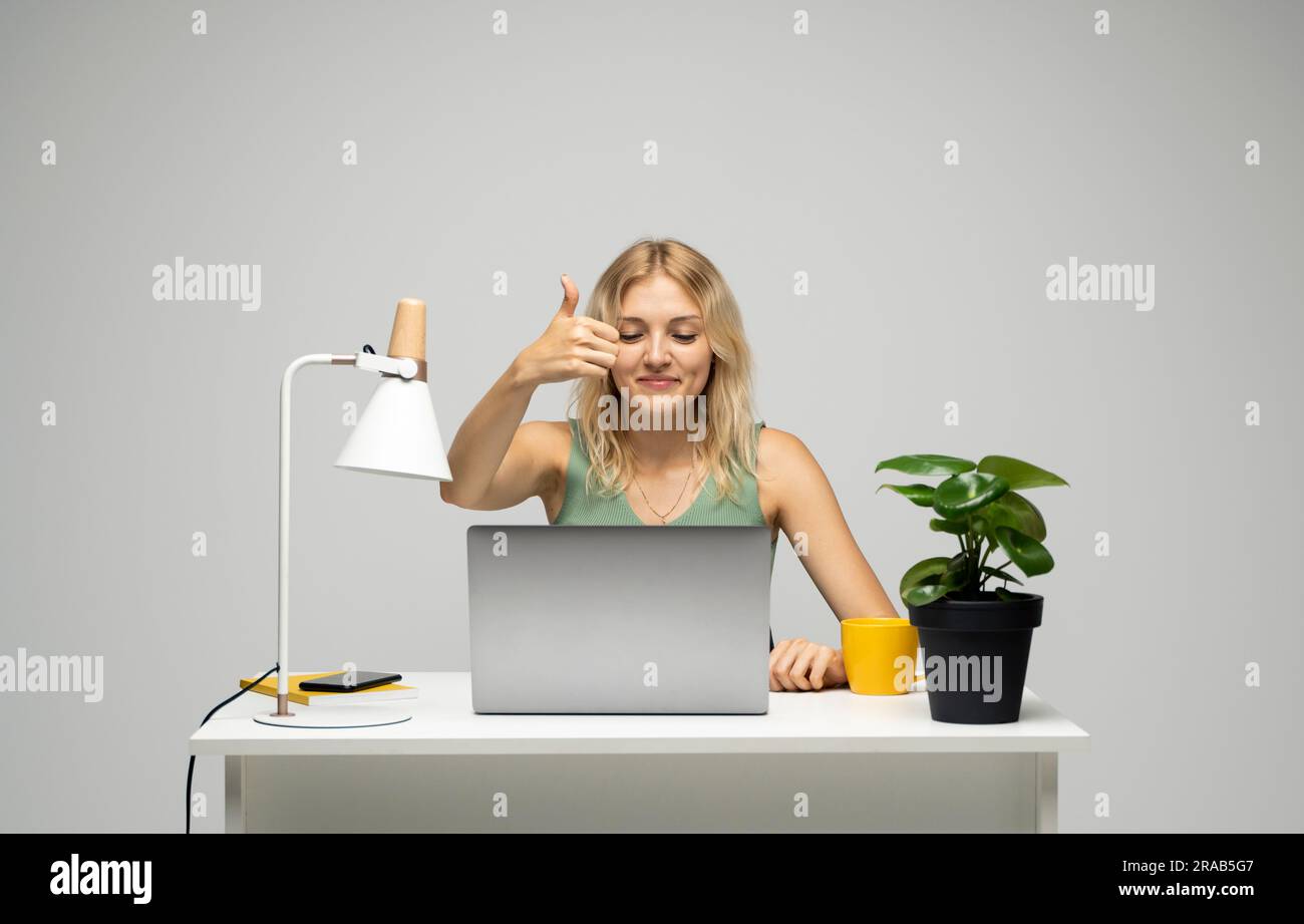 Cheerful blonde woman showing thumb up while looking in a laptop screen ...