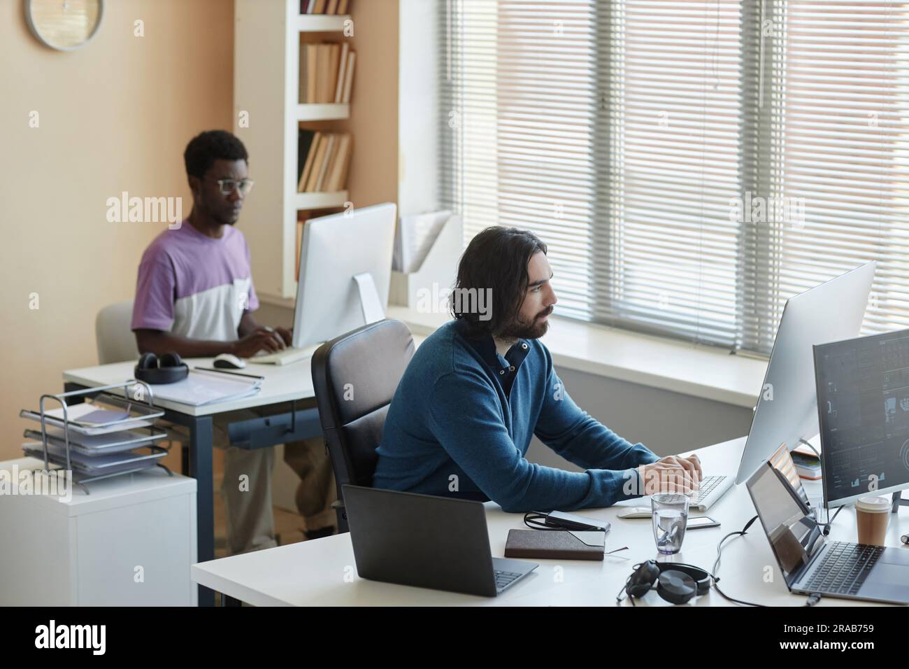 Young serious man pressing keys of computer keyboard while sitting by ...