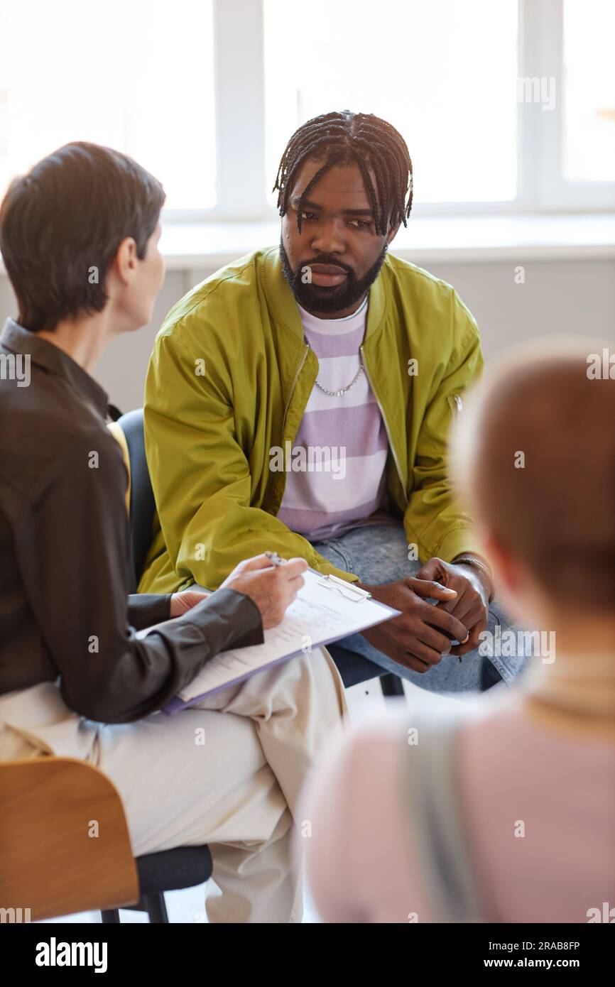 Vertical image of group of people talking to psychologist at session in ...