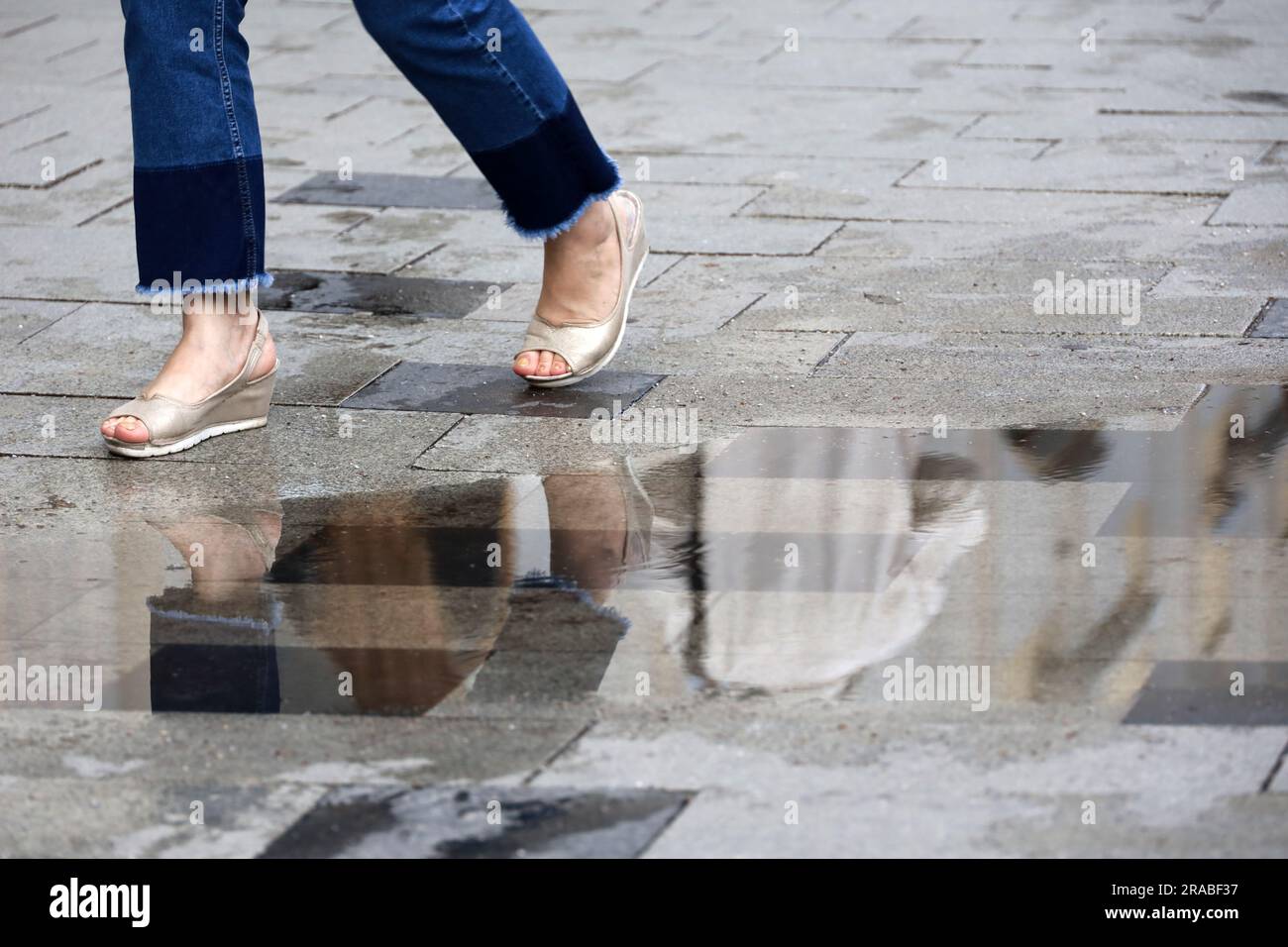 Female legs in jeans and shoes on wet sidewalk, woman run on a street ...