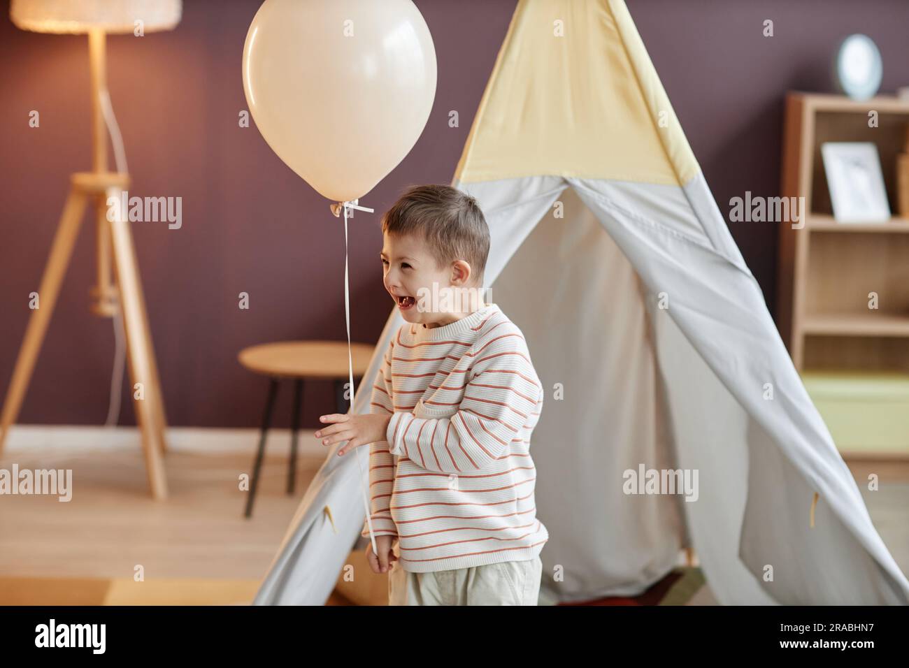 Portrait of cute little boy with down syndrome holding balloon while ...