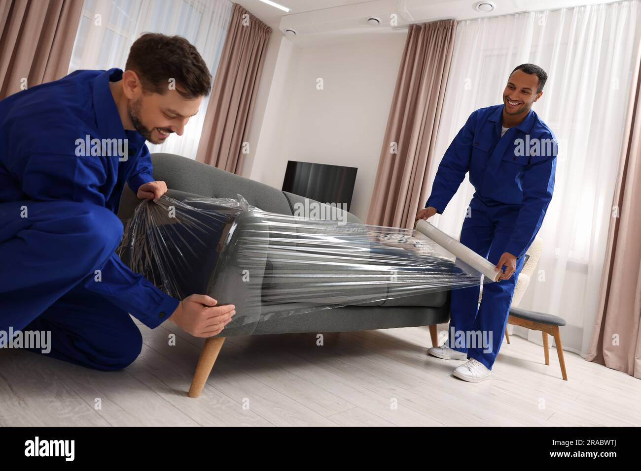 Male movers with stretch film wrapping sofa in new house Stock Photo ...