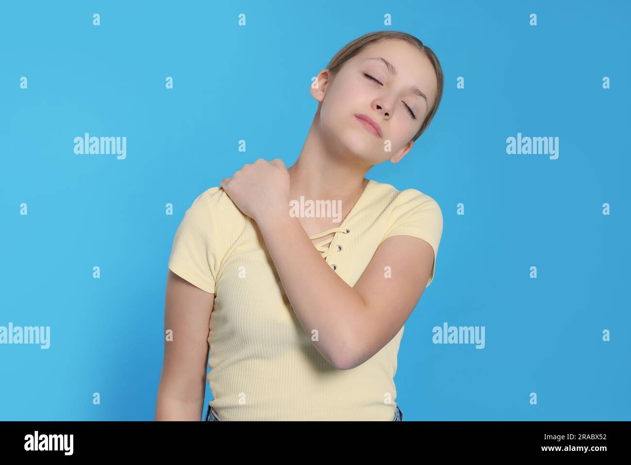Teenage girl suffering from pain in shoulder on light blue background ...
