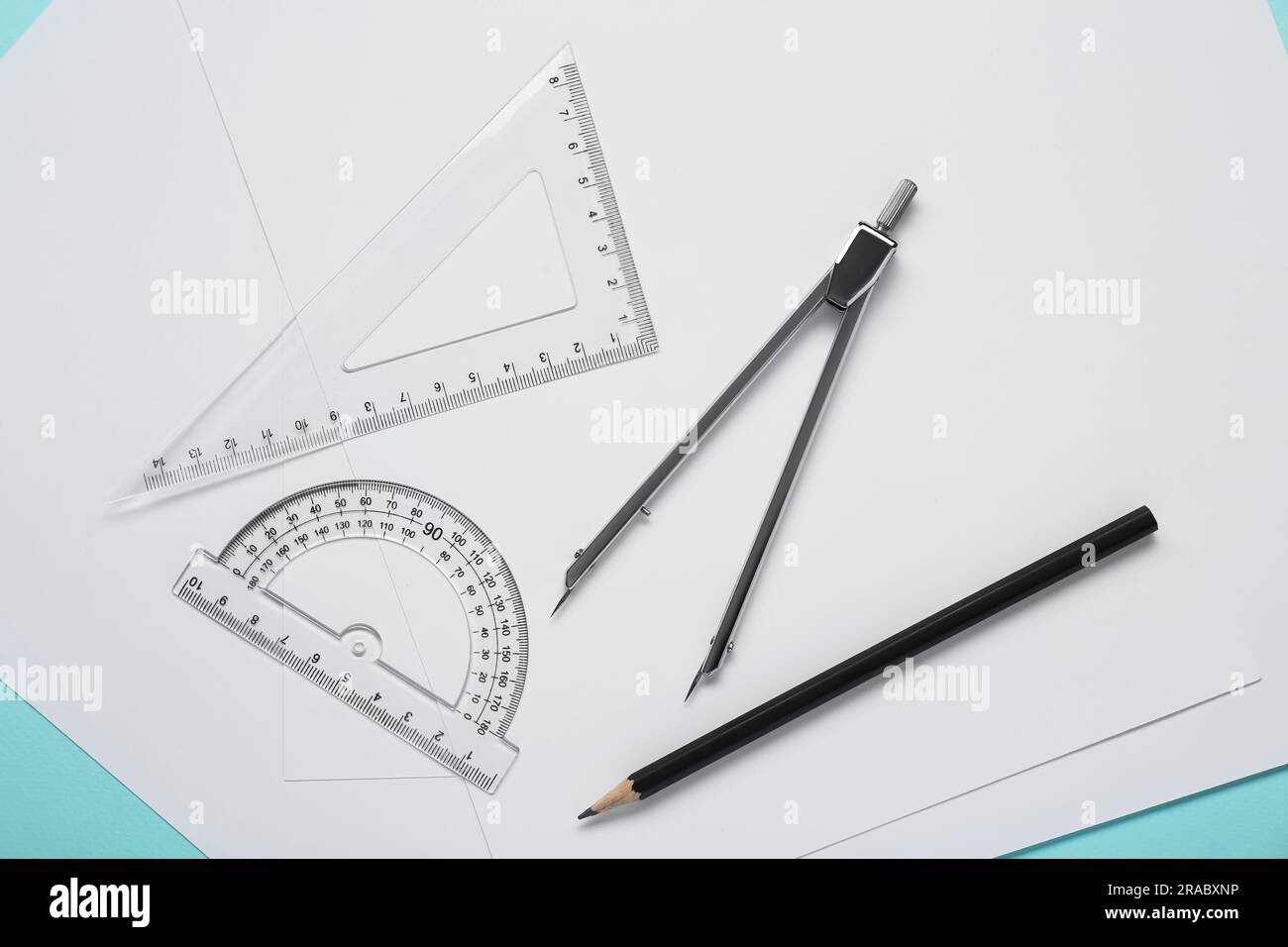 Different rulers, pencil, compass and paper sheets on turquoise ...