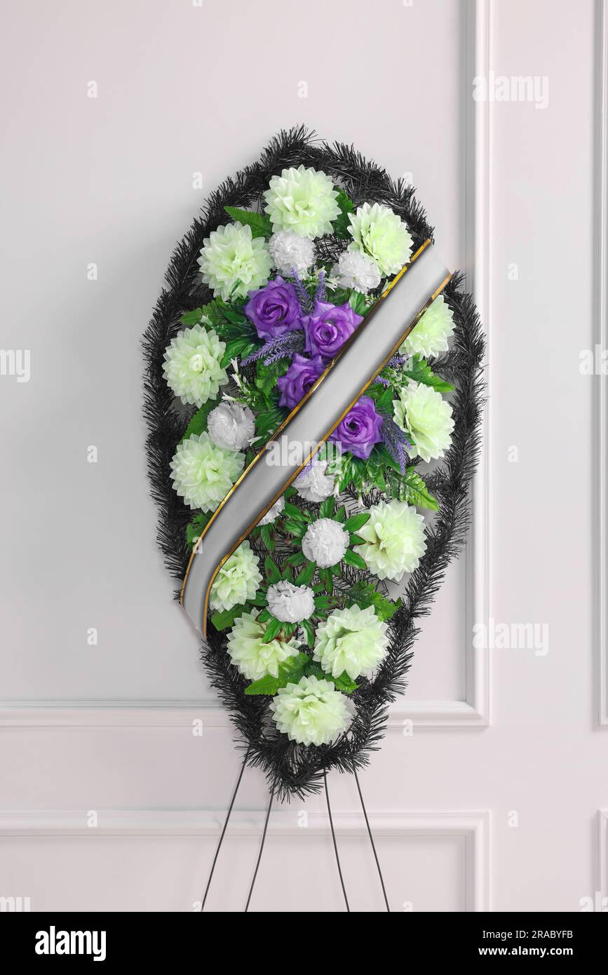 Funeral wreath of plastic flowers with ribbon near white wall Stock ...