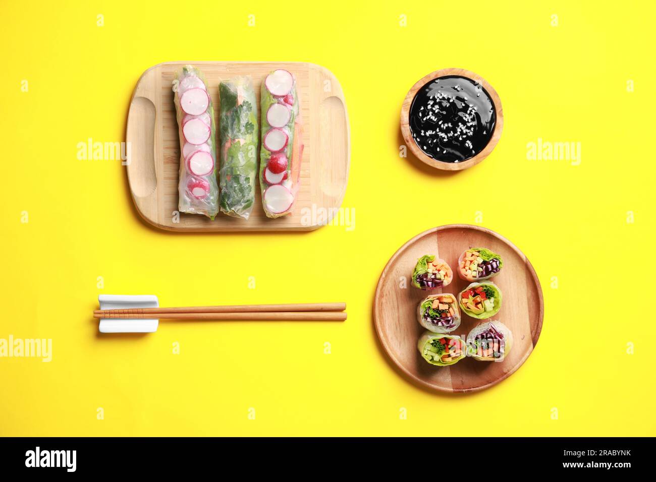 Different delicious spring rolls, chopsticks and soy sauce on yellow ...