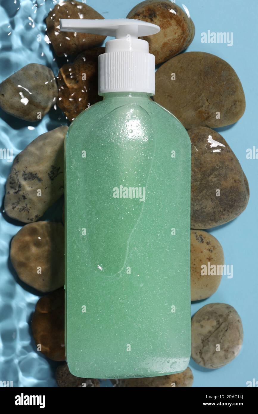Bottle of face cleansing product and stones in water against light blue ...