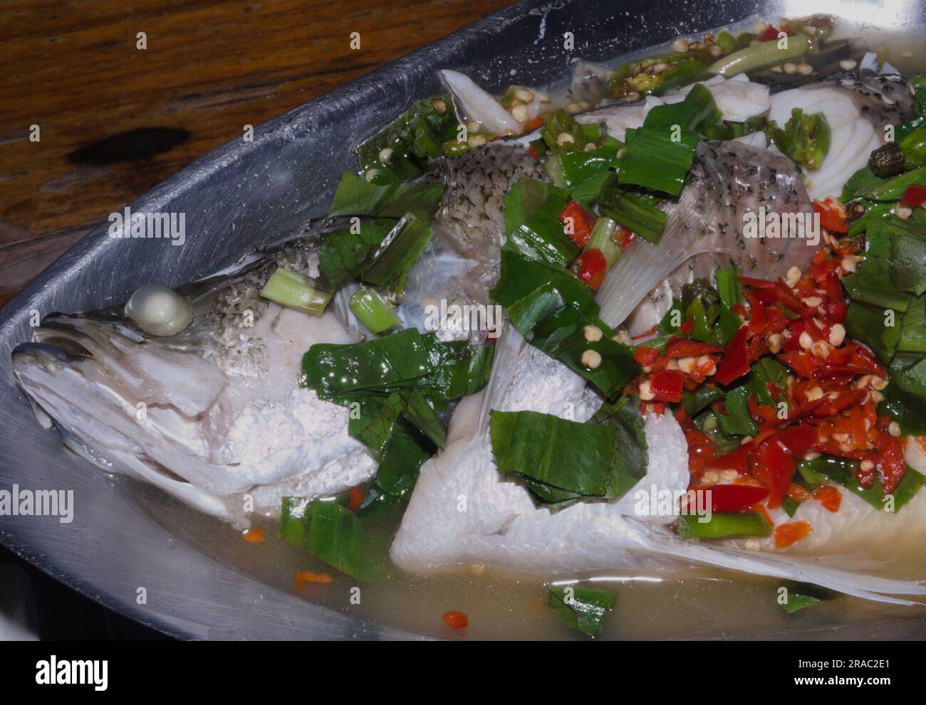 The head of a spicy sea bass fish with limes on a metal tray ready to ...