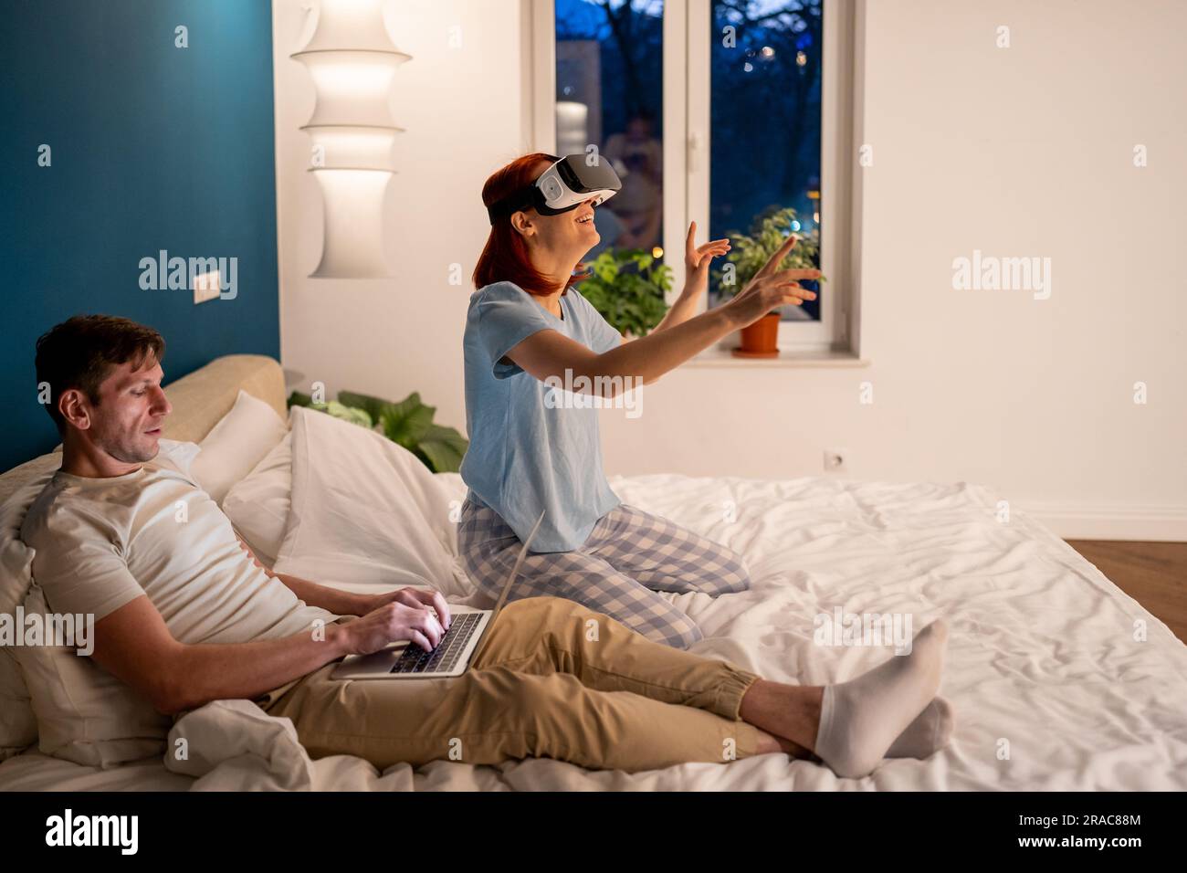 Focused boyfriend sits on bed with laptop near girlfriend playing ...